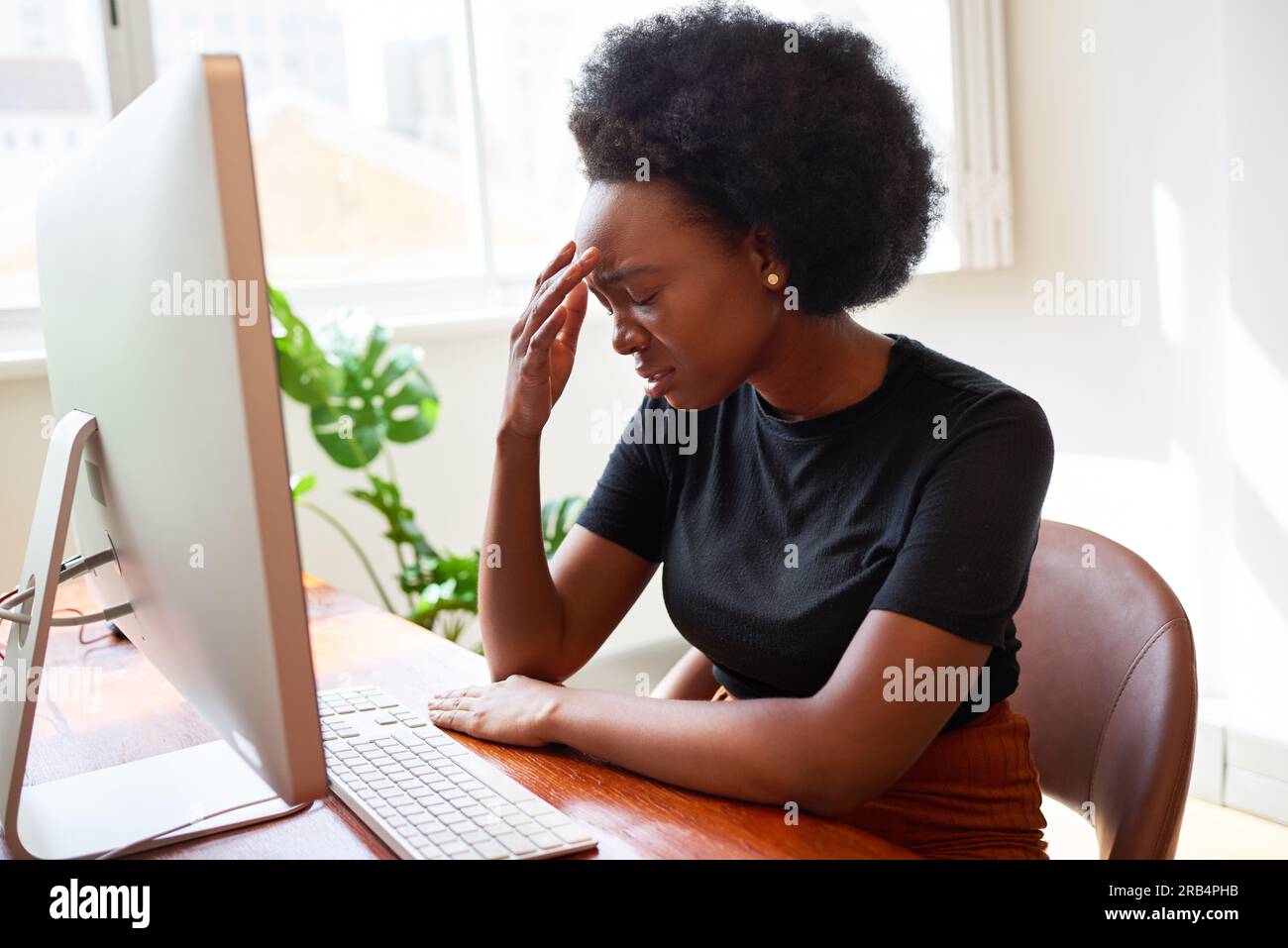 Tired and upset young developer sits with head in hands at desk, Black ...