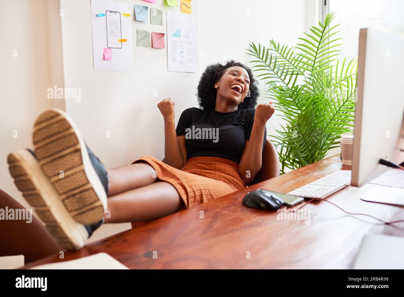 Beautiful young Black woman in tech cheers, feet on desk relaxing Stock ...