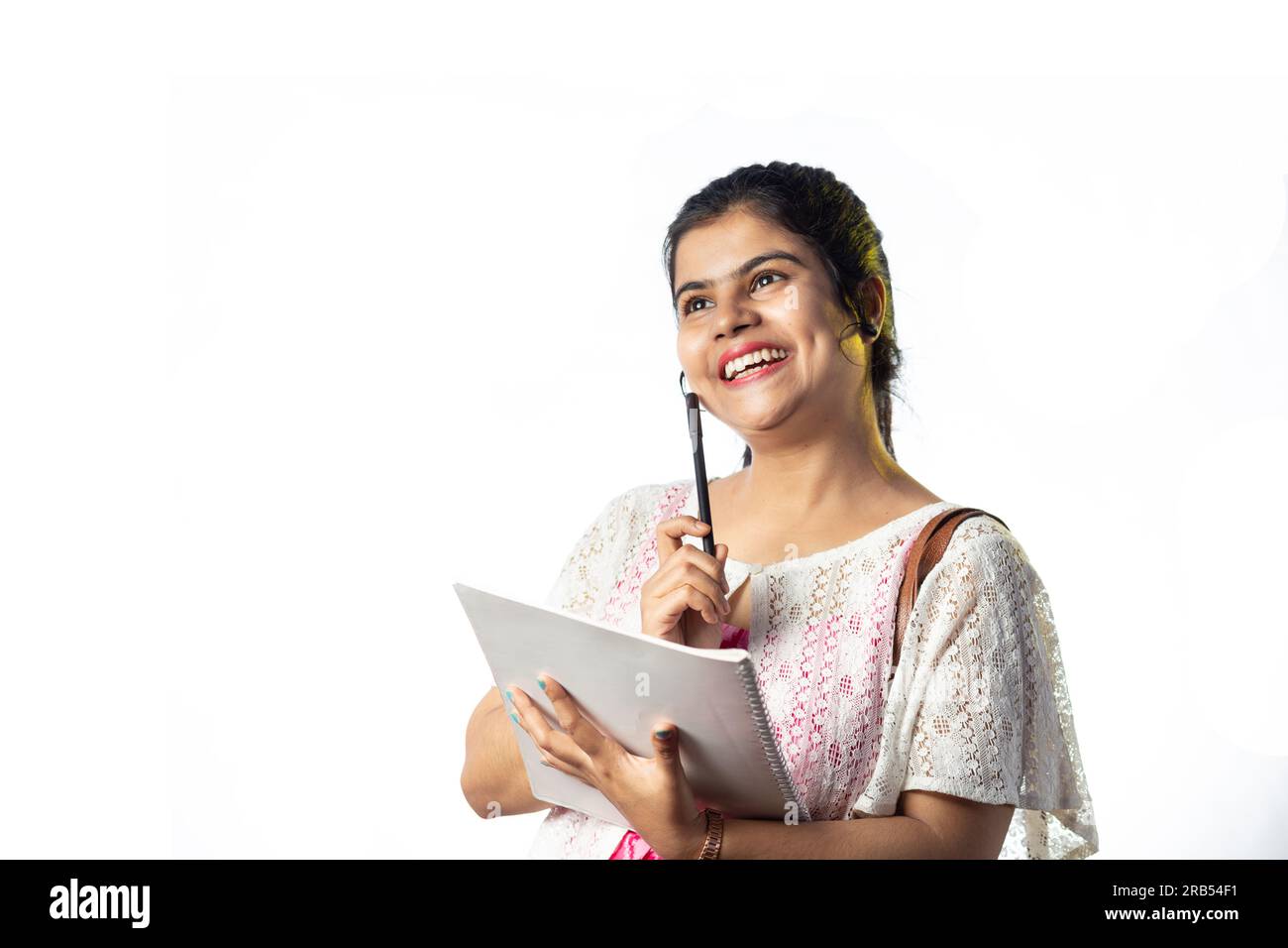 A pretty young Indian girl thinking while taking notes and looking ...