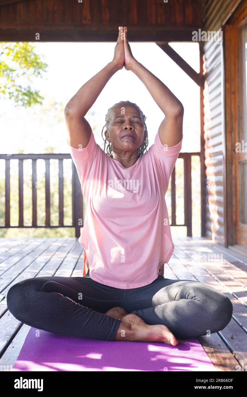 Focused senior african american woman practicing yoga on mat on terrace ...