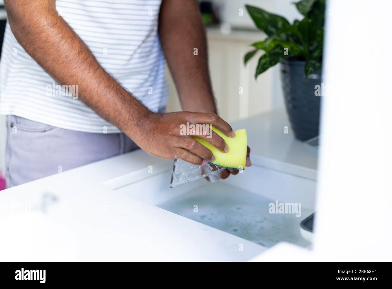 Midsection of biracial man washing up dishes in kitchen sink. Healthy ...