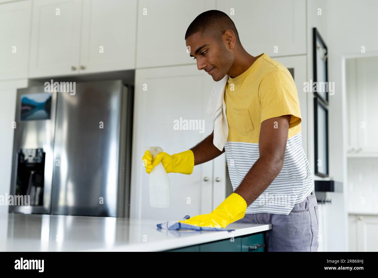 Happy biracial man spraying and cleaning worktop in sunny kitchen ...