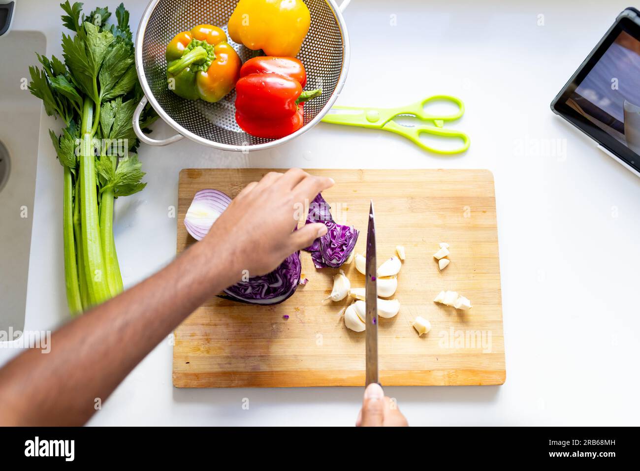 Hands of biracial man chopping vegetables and using tablet in sunny ...