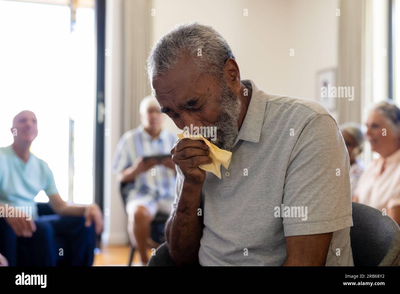Distressed senior biracial man holding tissue and crying in group ...
