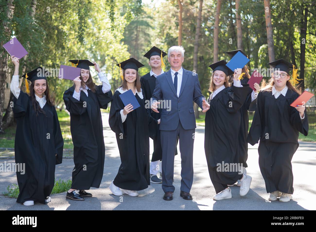 A university professor and seven robed graduates are jumping outdoors ...