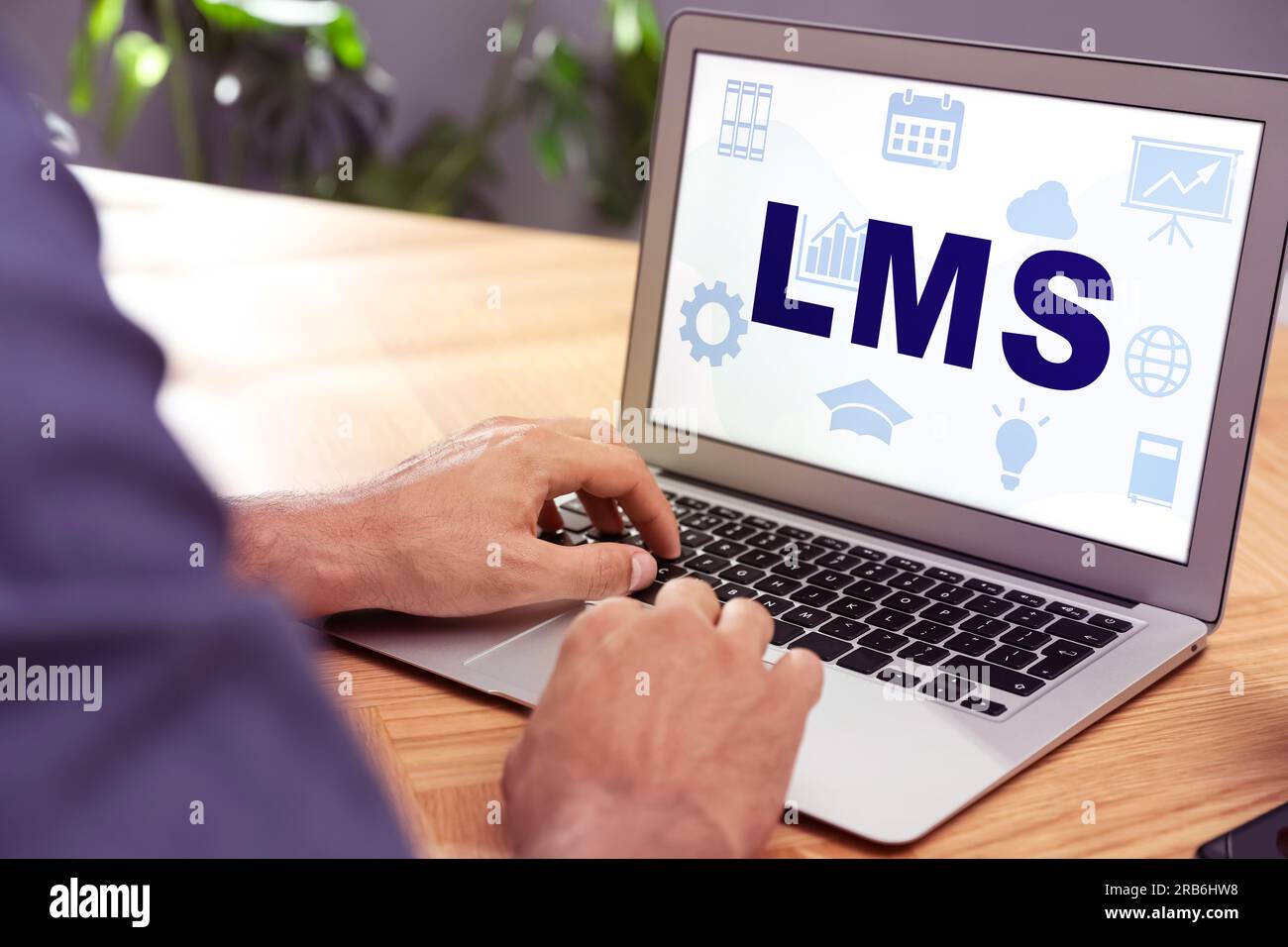 Learning management system. Man using modern laptop at wooden table, closeup. Different icons ...