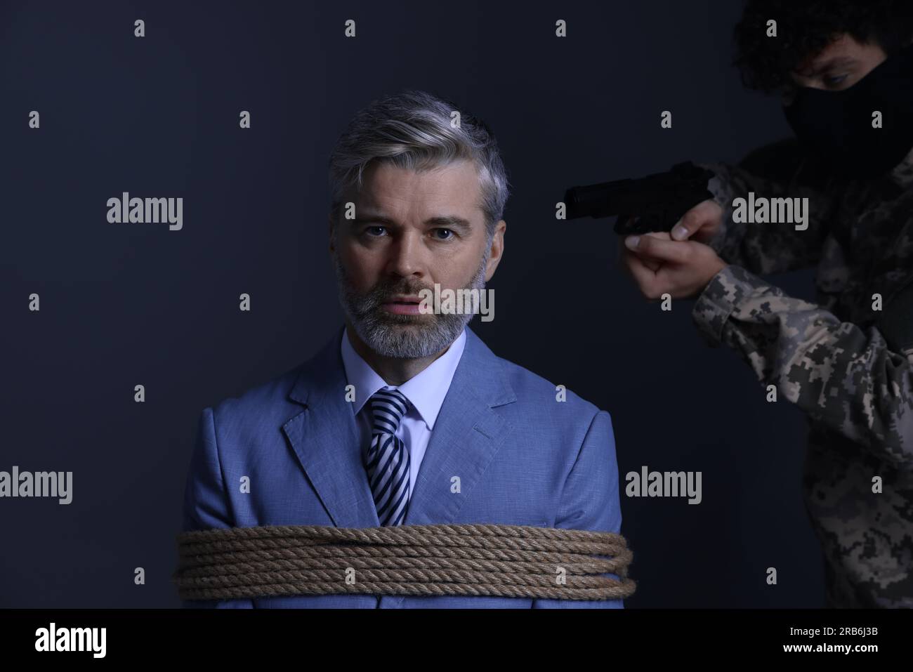 Kidnapper aiming gun at tied victim on dark background. Hostage taking ...