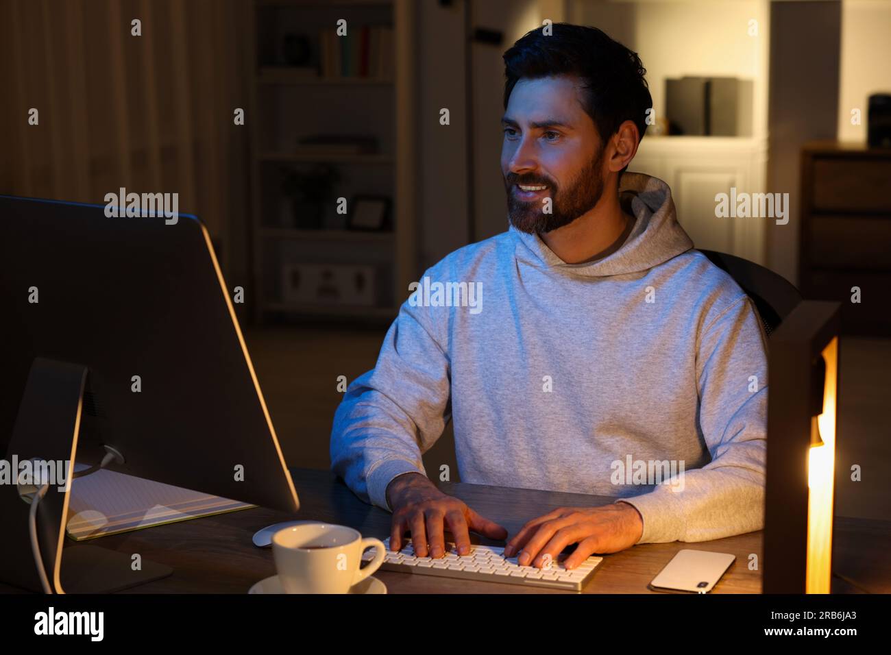 Home workplace. Happy man working with computer at wooden desk in room ...