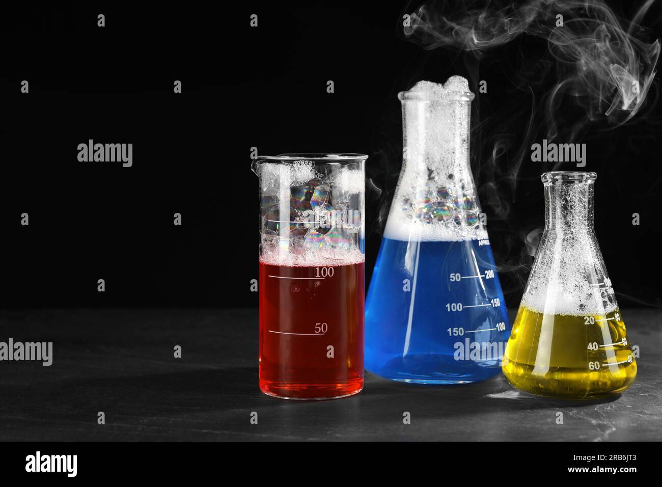 Laboratory glassware with colorful liquids and steam on dark table ...