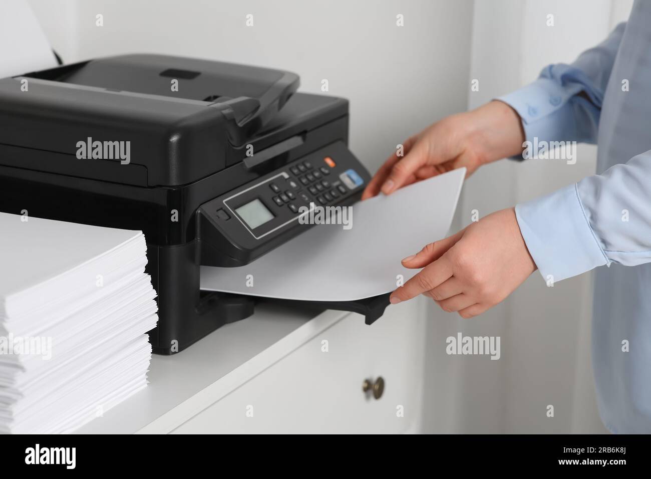 Woman loading paper into printer at white chest of drawers indoors ...