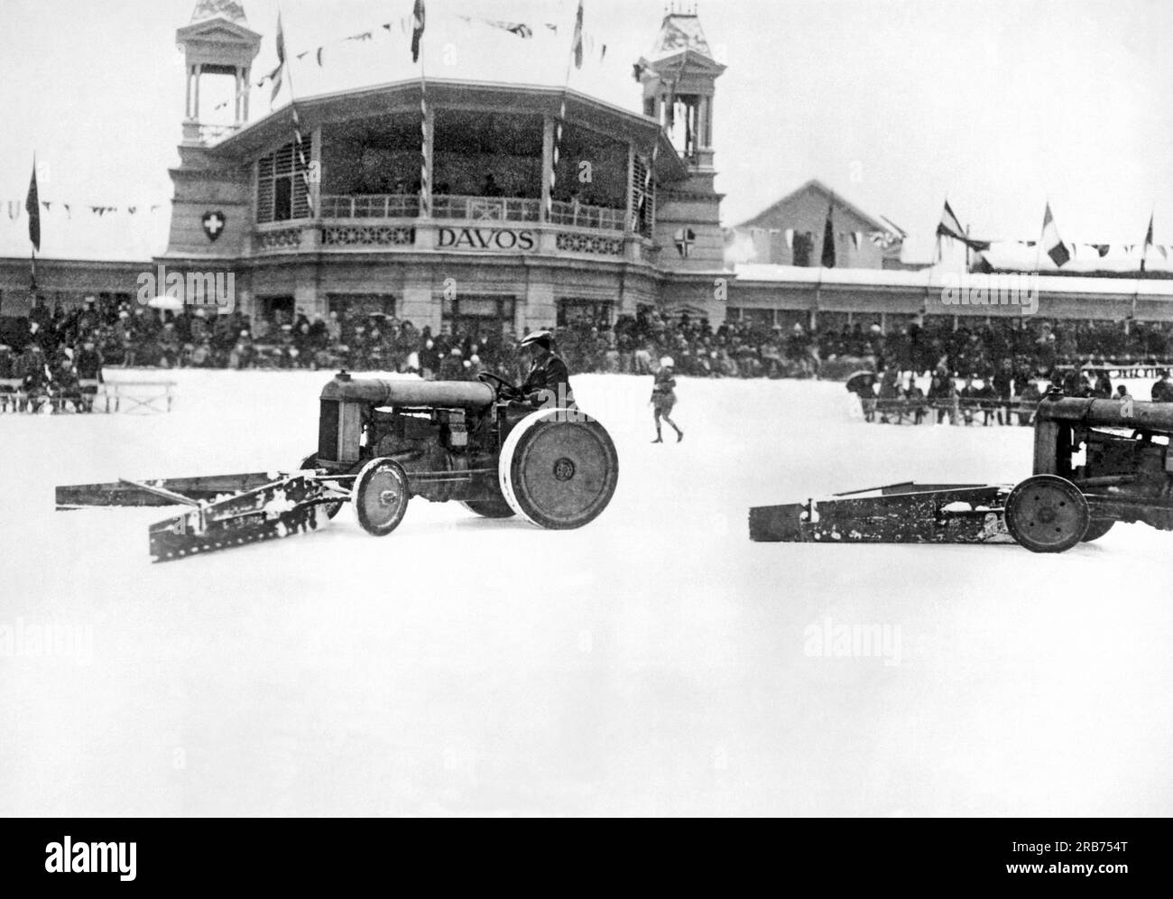 Davos, Switzerland: 1928. Tractors clear the snow off the ice rink at ...