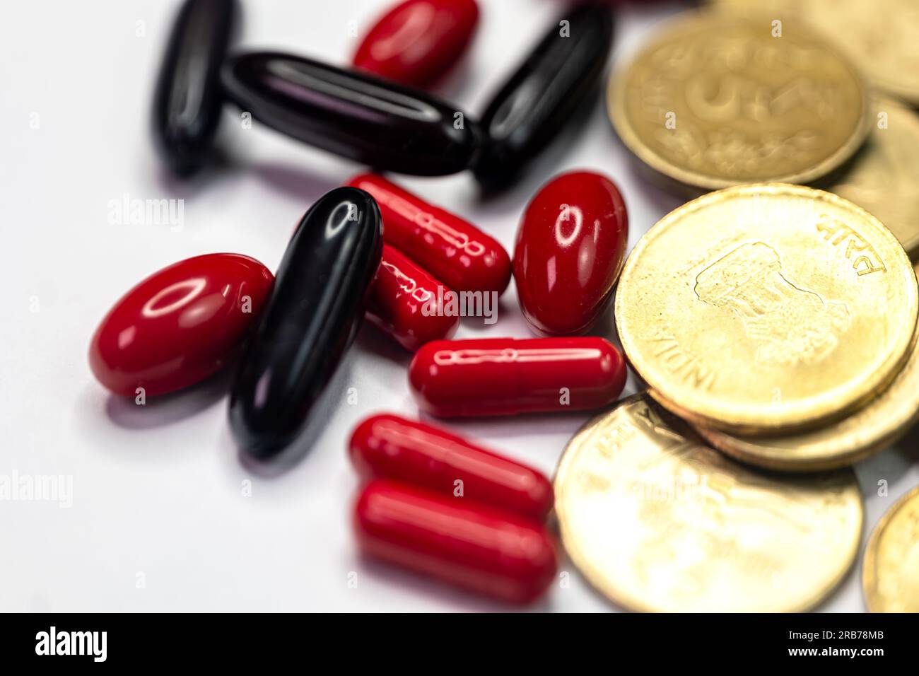 A close-up of Indian 5 rupees coins and red and black pills on a white ...