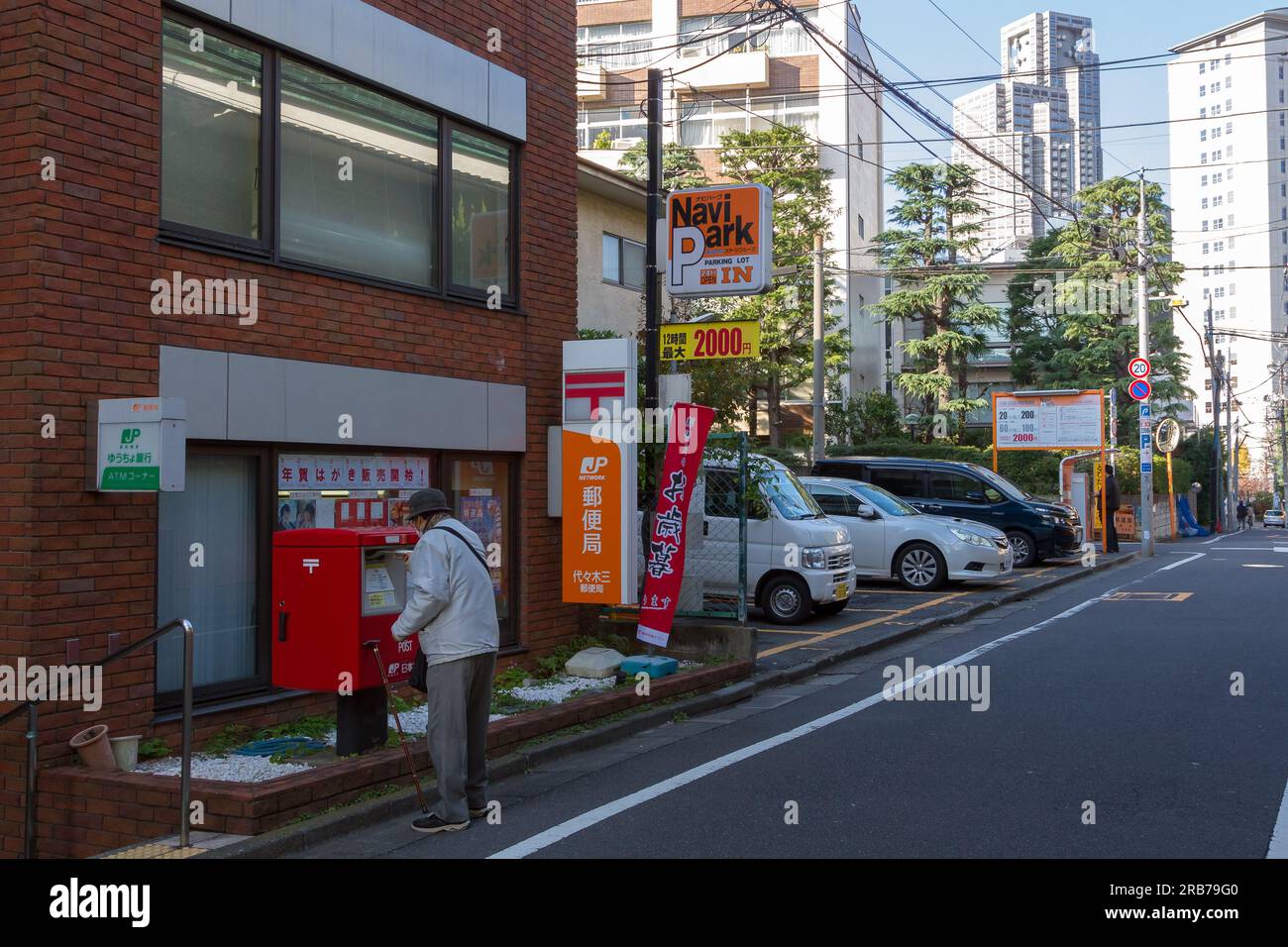 An older Japanese man post mail in a post box outside a small Post ...