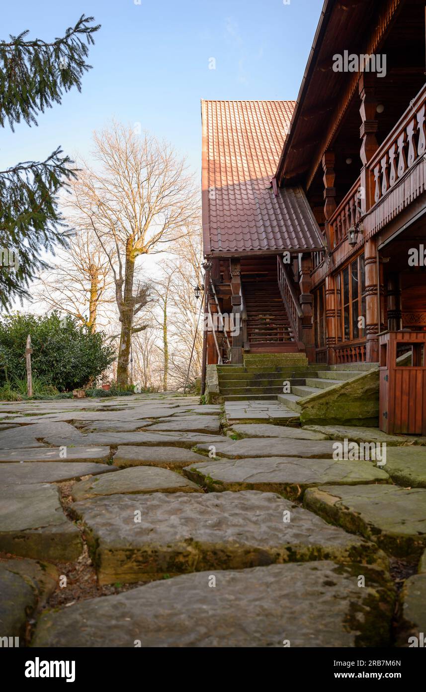A fragment of a country wooden house with a carved balcony and a paved ...
