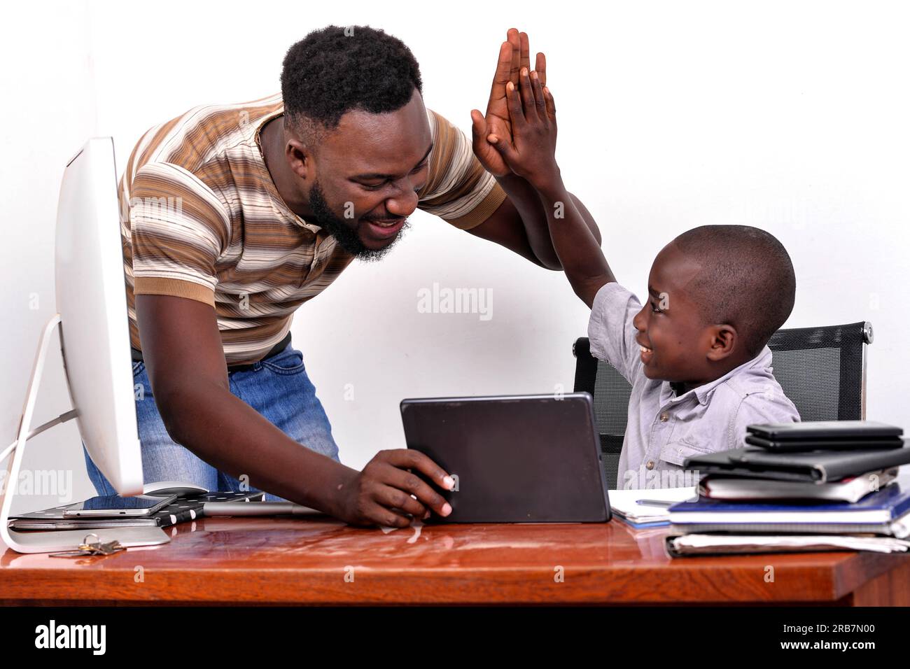 a young dad and his son in an office with tablet clapping their palms ...