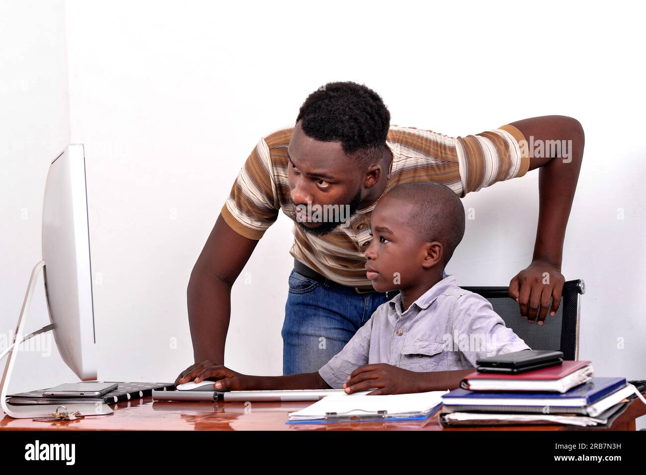 a young father in a T-shirt standing in office guiding his son to work ...