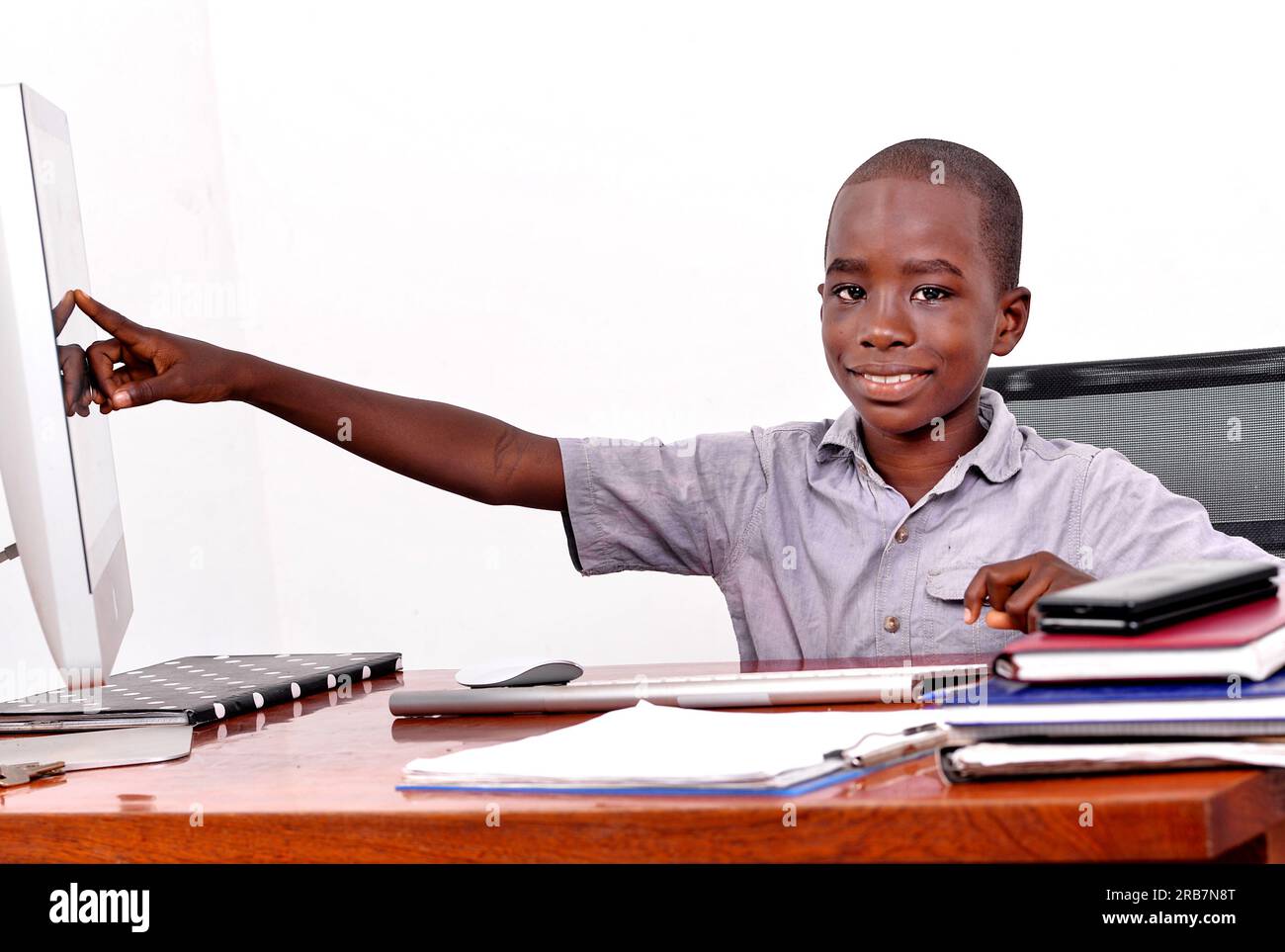a young boy sitting in a desk showing the computer screen and looking ...