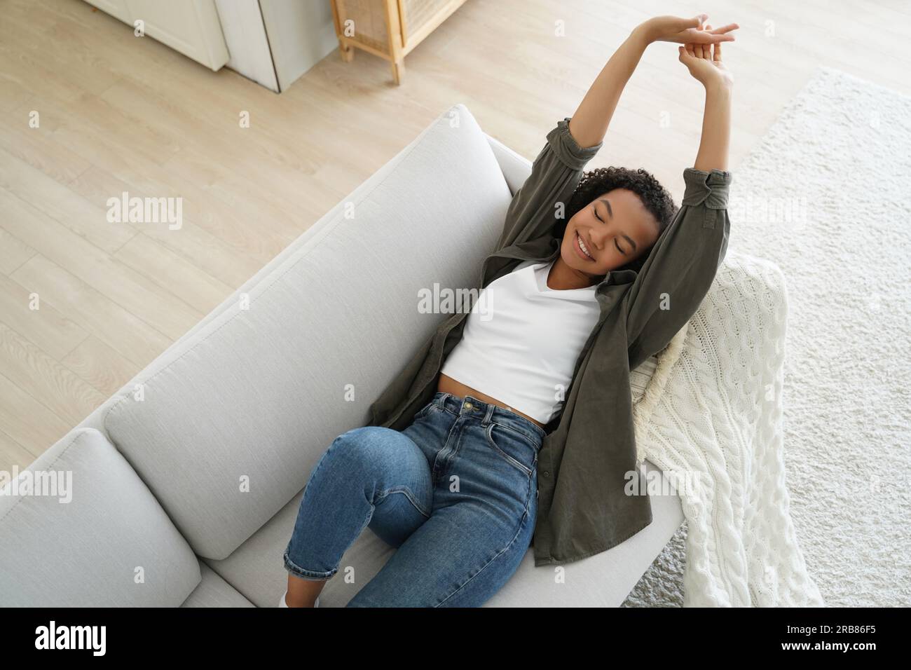 Smiling girl stretches after nap on comfy sofa at home. Happy teen ...
