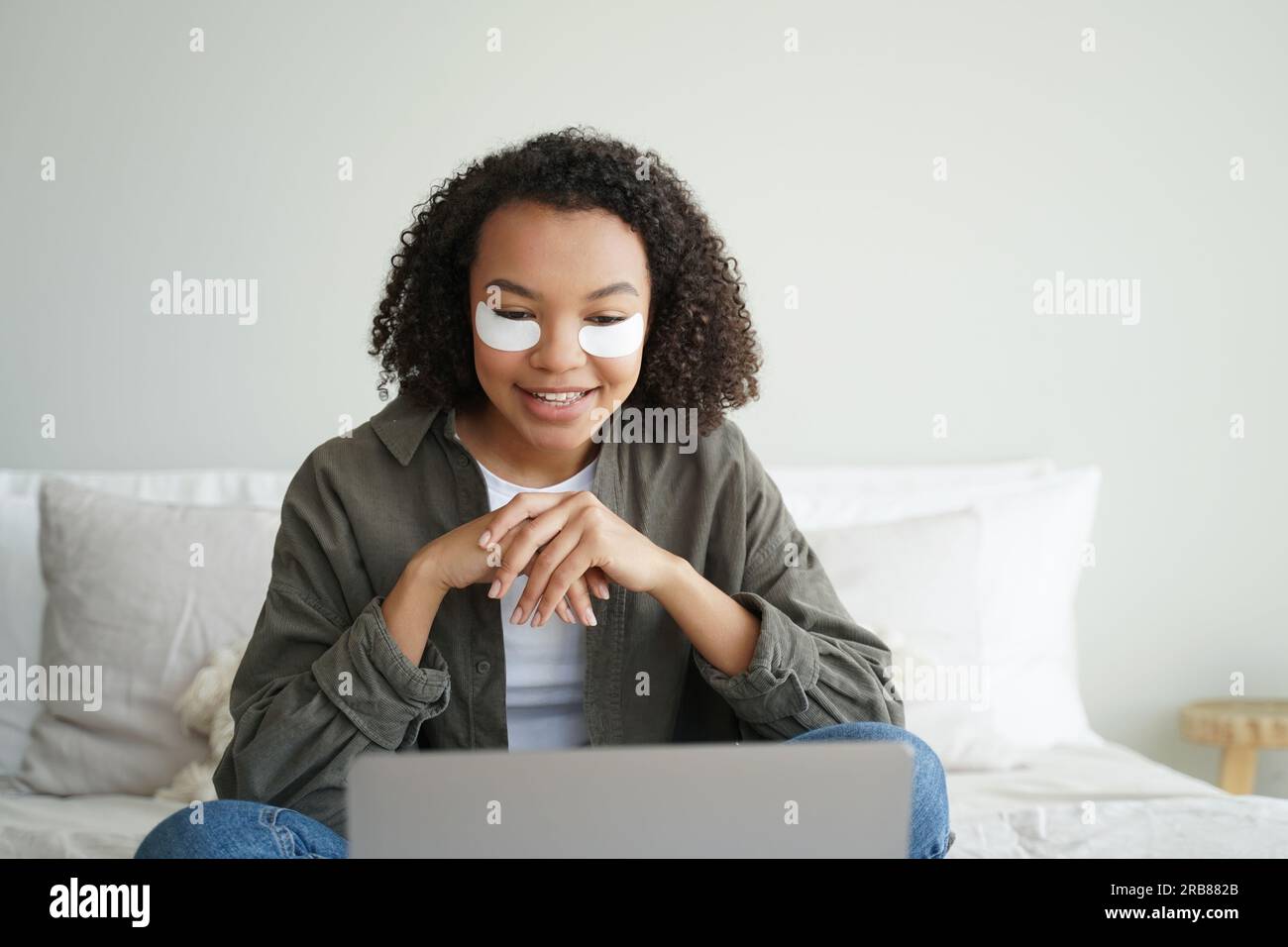 Biracial girl with under-eye patches working on laptop. Lady watching ...