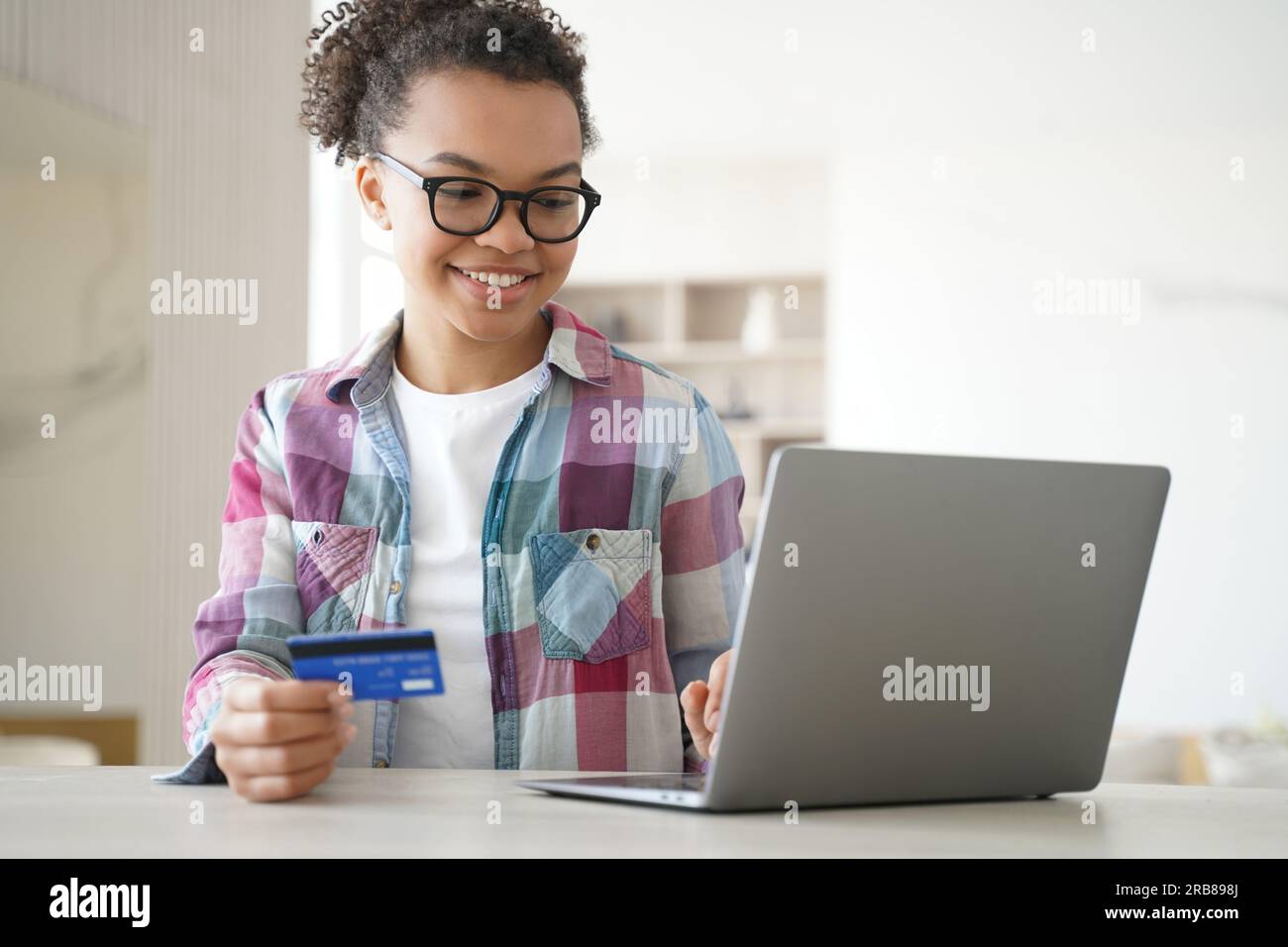 Biracial teen girl smiles, shops online with bank card, laptop. E ...