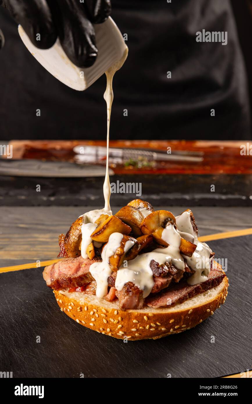Cook preparing burger adding the sauce. The process of making a burger ...