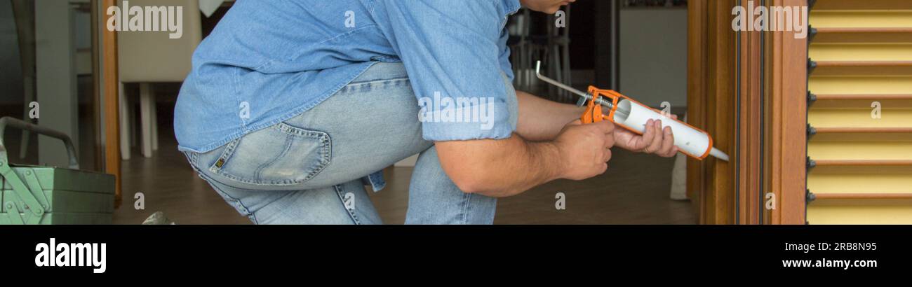 Image of the hands of a handyman who with a silicone gun installs and ...