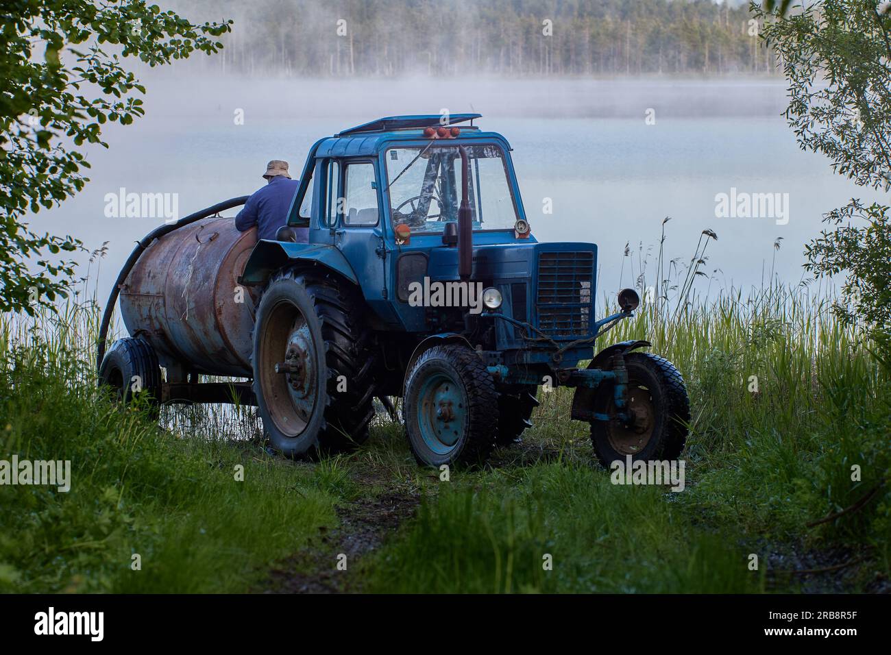 Farmer draws water from lake into tanker attached to wheeled tractor ...