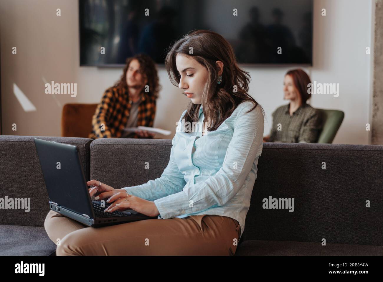 Front view photo of girl working on lap top while sitting on a grey ...