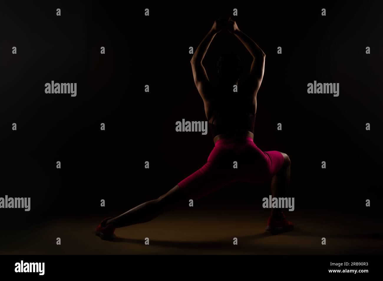 20s woman crouching and stretching her left leg. Arms up.. Back view ...