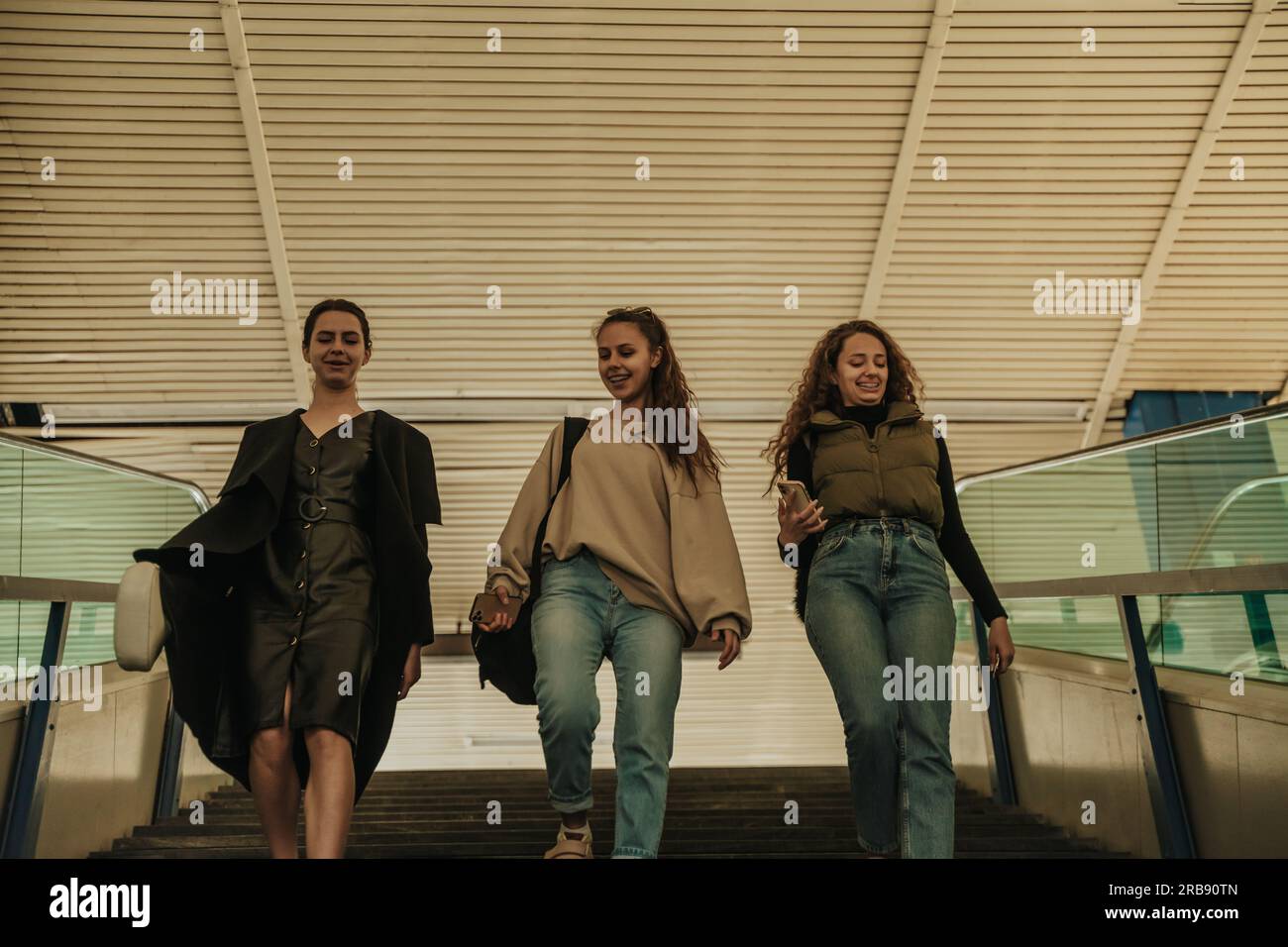 Three female friends walking downstairs at the shopping mall while ...