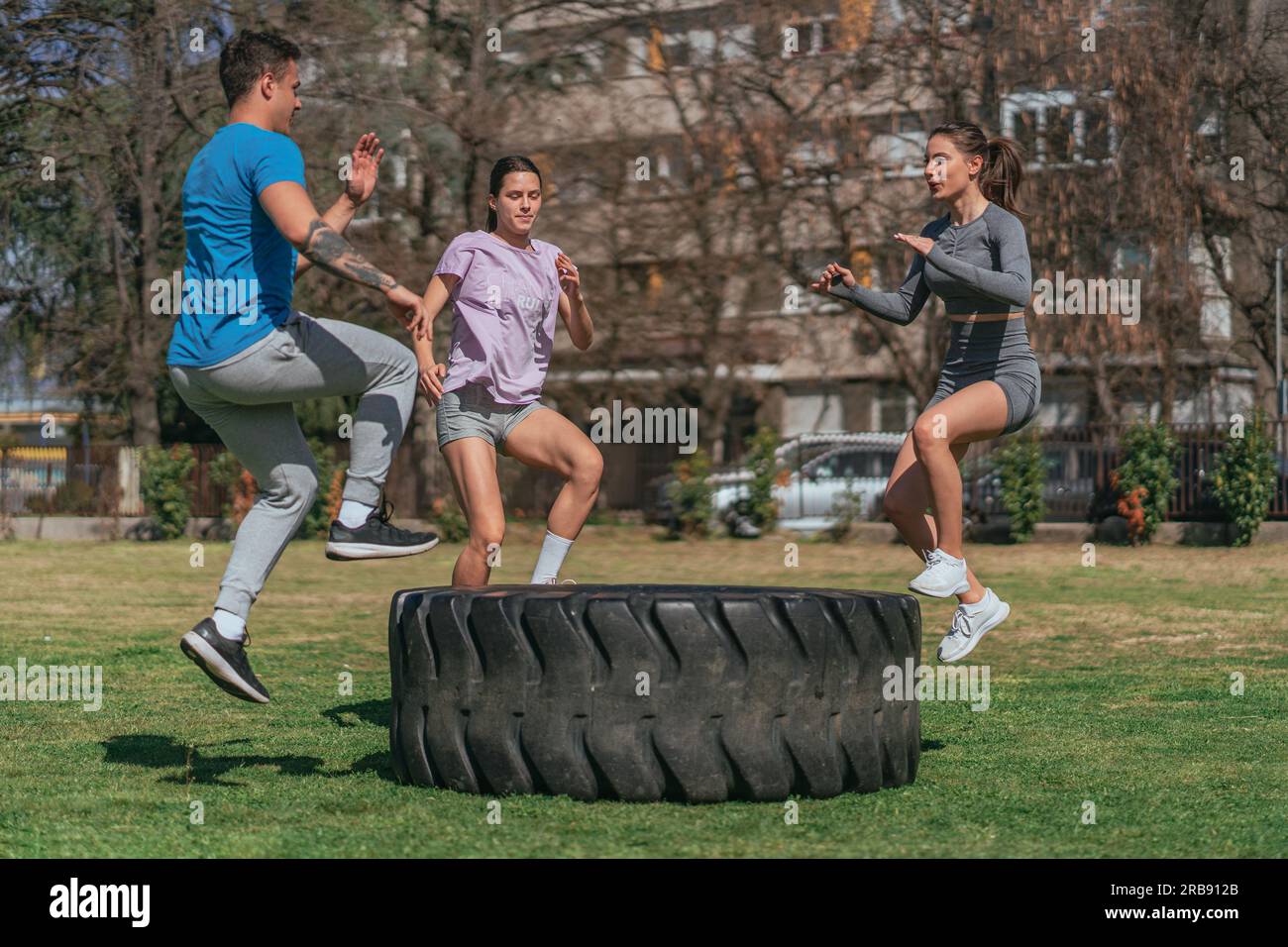 Beautiful, young sports people jumping on big truck tire in the park ...