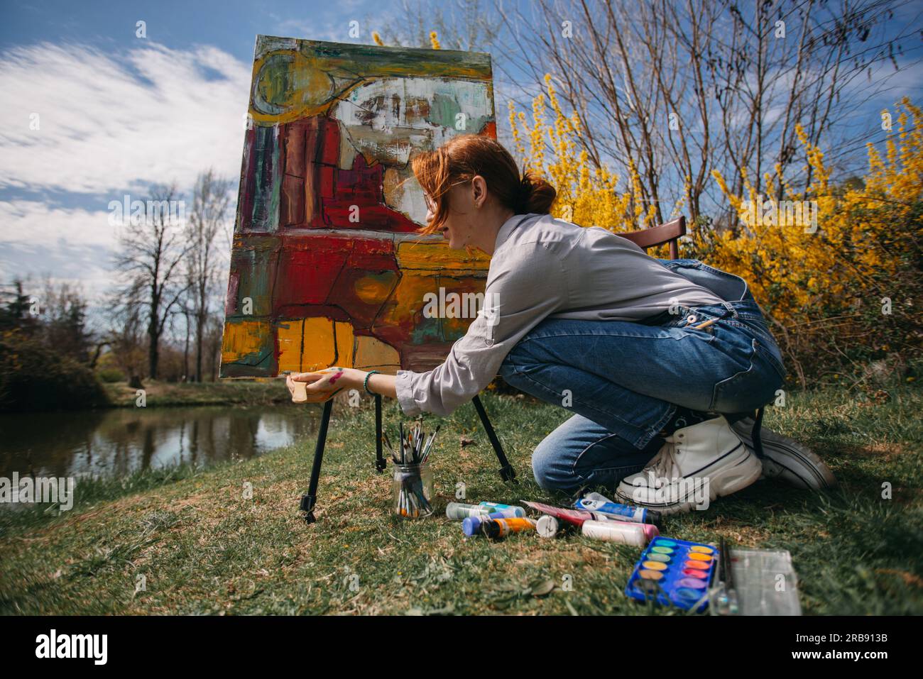 Red haired girl with bun painting on big canvas a colorful picture in ...