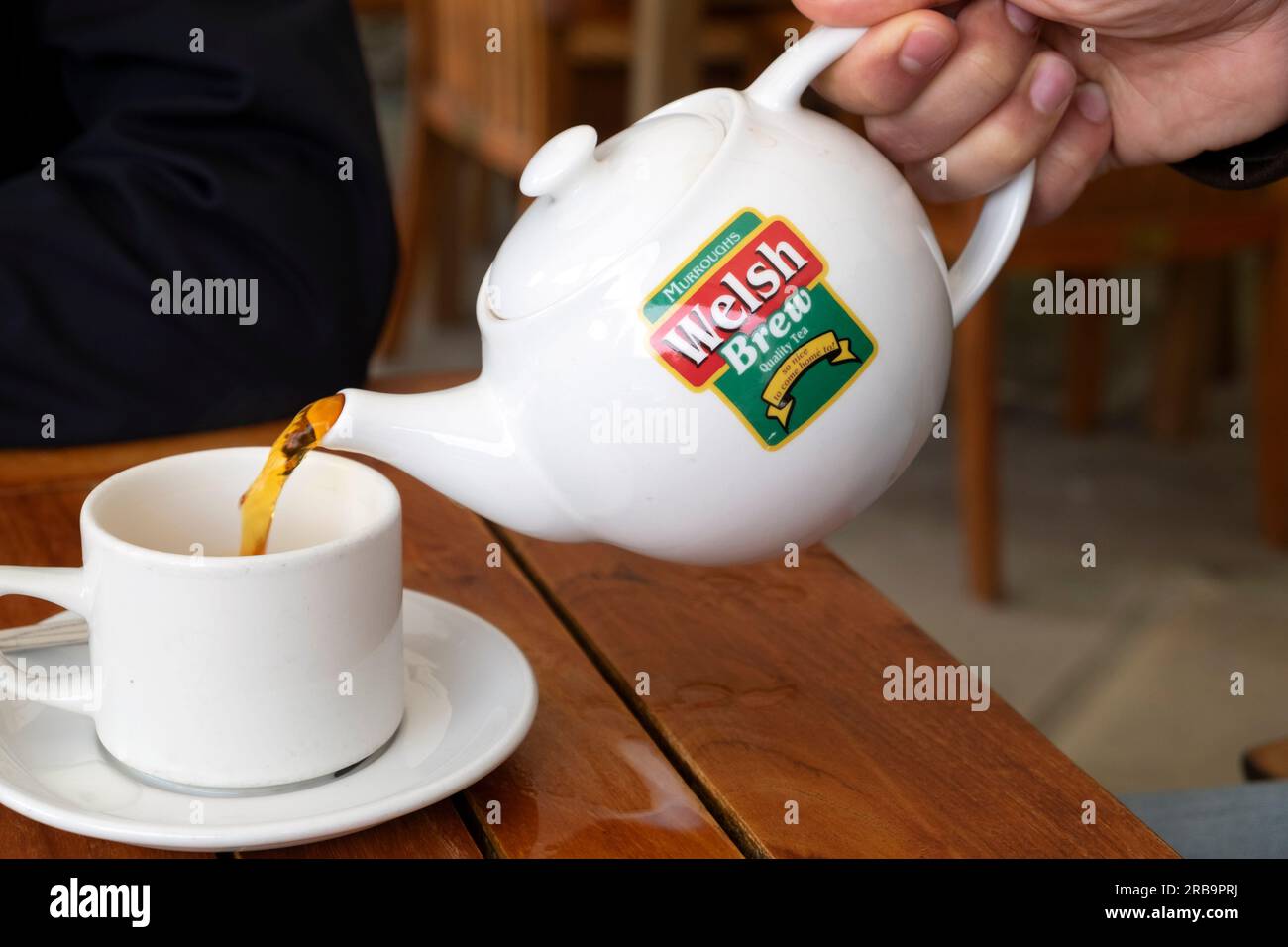 Hand holding handle of Welsh teapot pouring tea into cup and saucer on ...