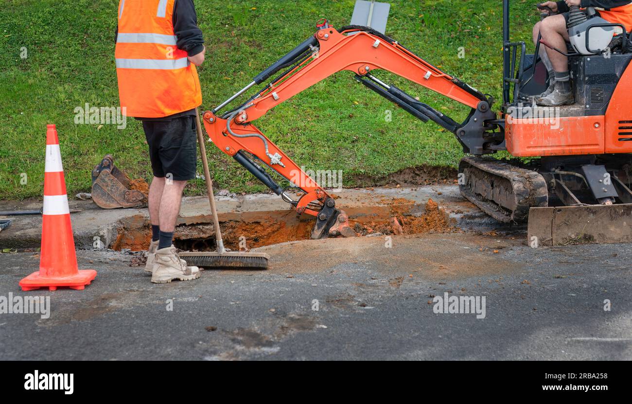 Man driving excavator, digging up dirt between cut concrete pavement ...