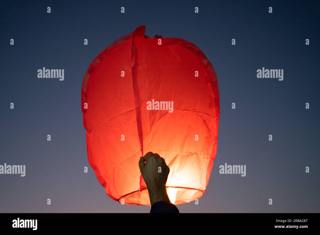hand holding large paper sky lantern with candle burning at bottom and ...