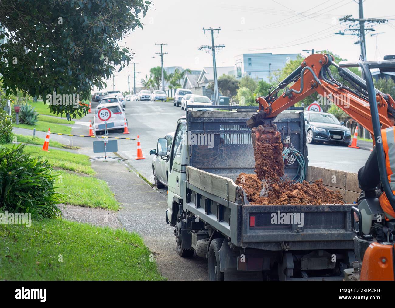Excavator digging up dirt and moving into truck. Traffic cone and cars ...