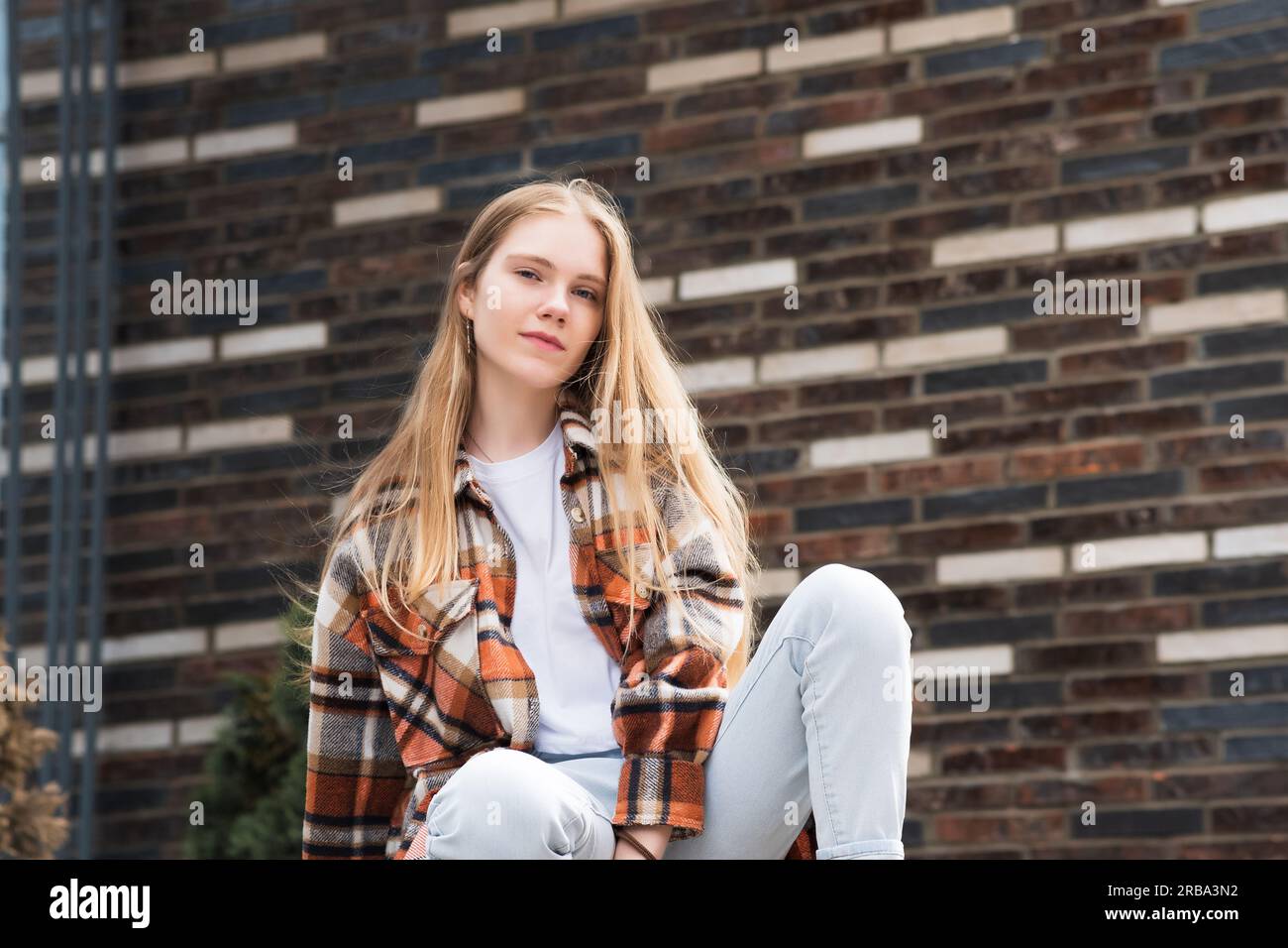 young woman sitting near brick wall of city building Stock Photo - Alamy