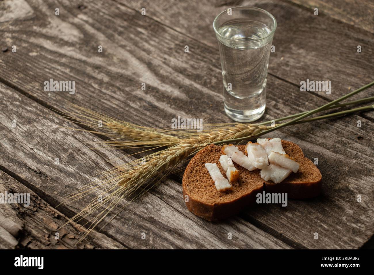 a glass of vodka next to a piece of black bread with bacon on a wooden ...