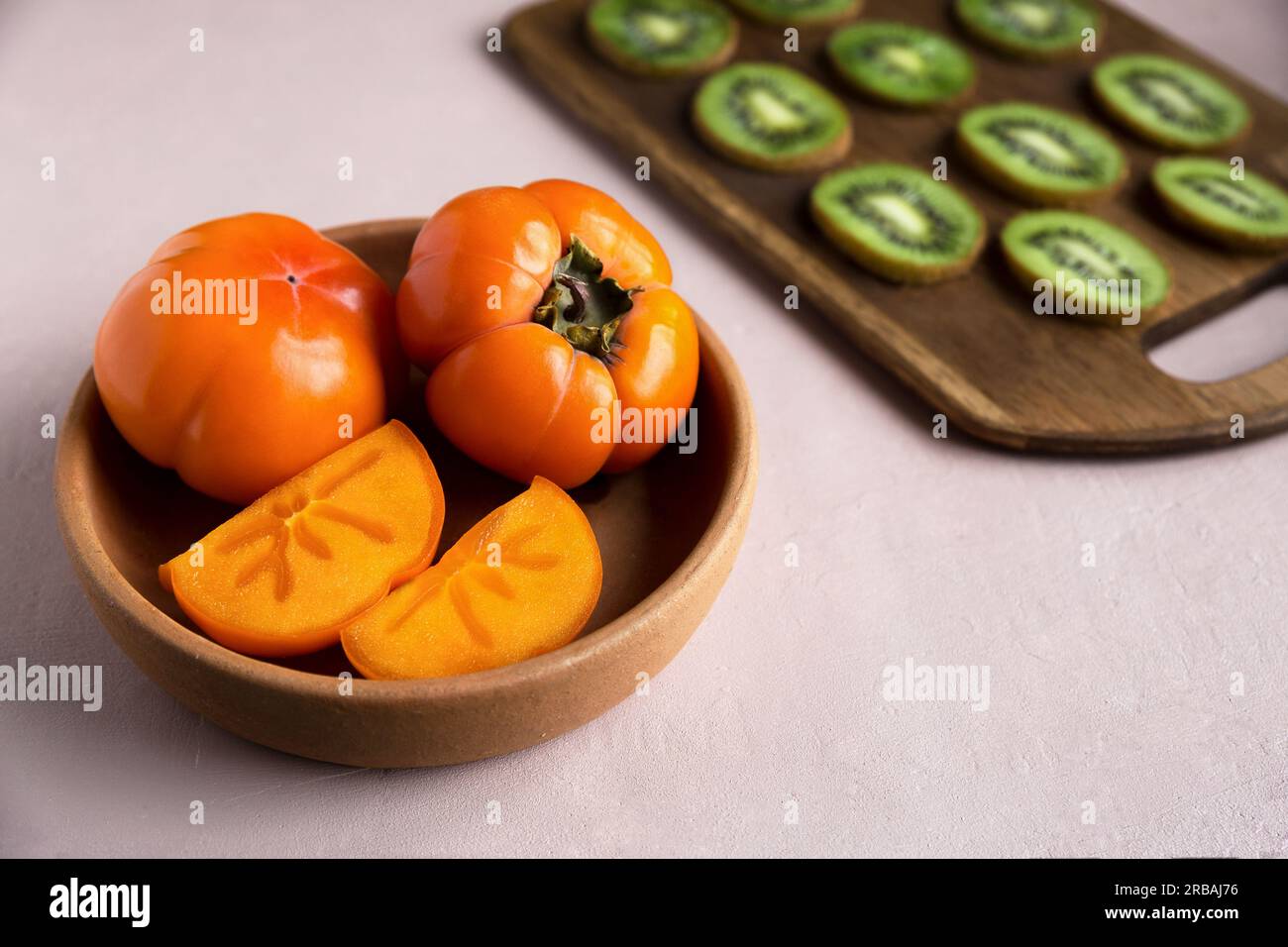 Ripe orange persimmons lies in a clay plate on a pink background next ...