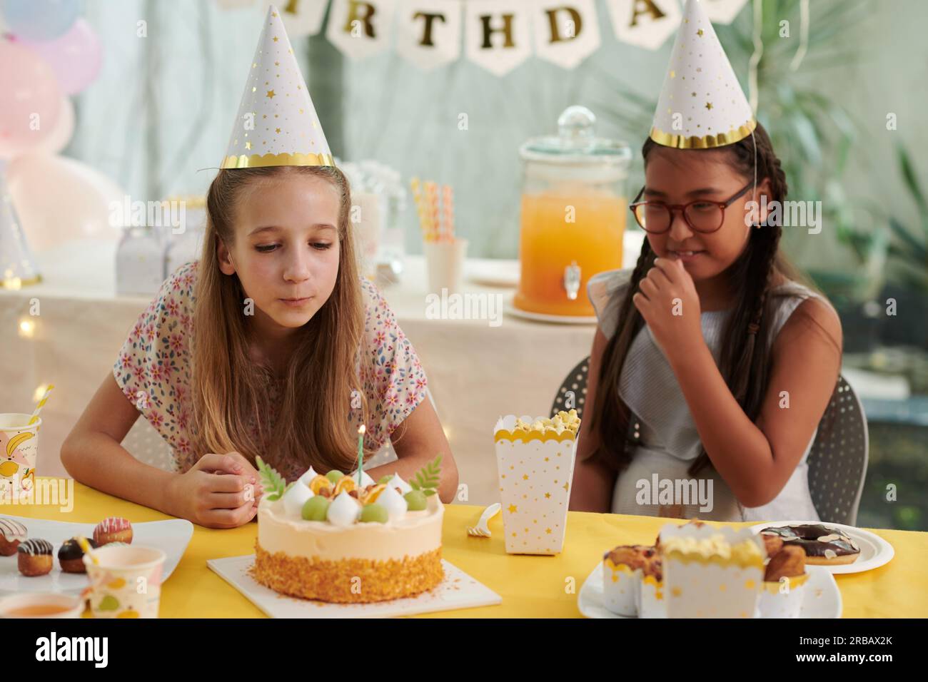 Girl in party hat blowing candle on birthday cake Stock Photo - Alamy