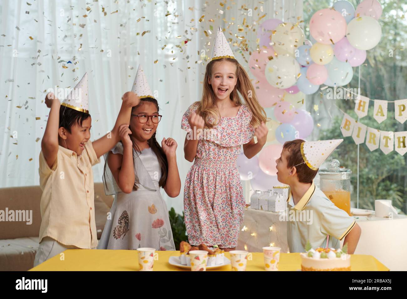 Group of kids jumping under falling confetti at birthday party Stock ...