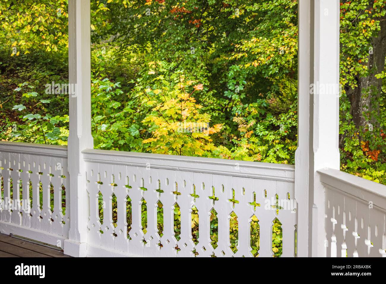 Railing on a veranda with wooden carpentry by a deciduous trees with ...