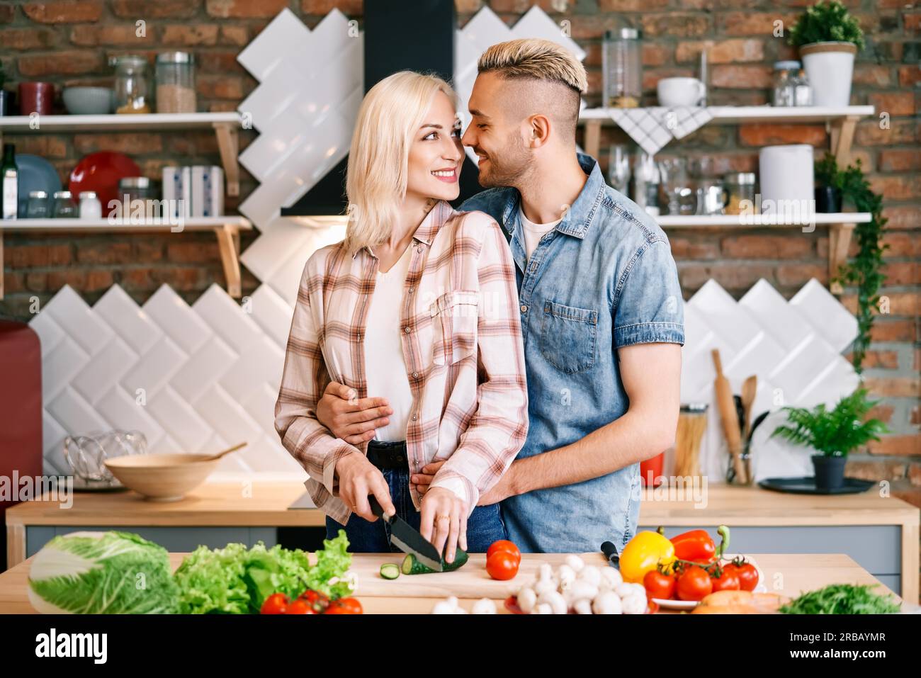 Smiling young couple cooking together vegetarian meal in the kitchen at ...