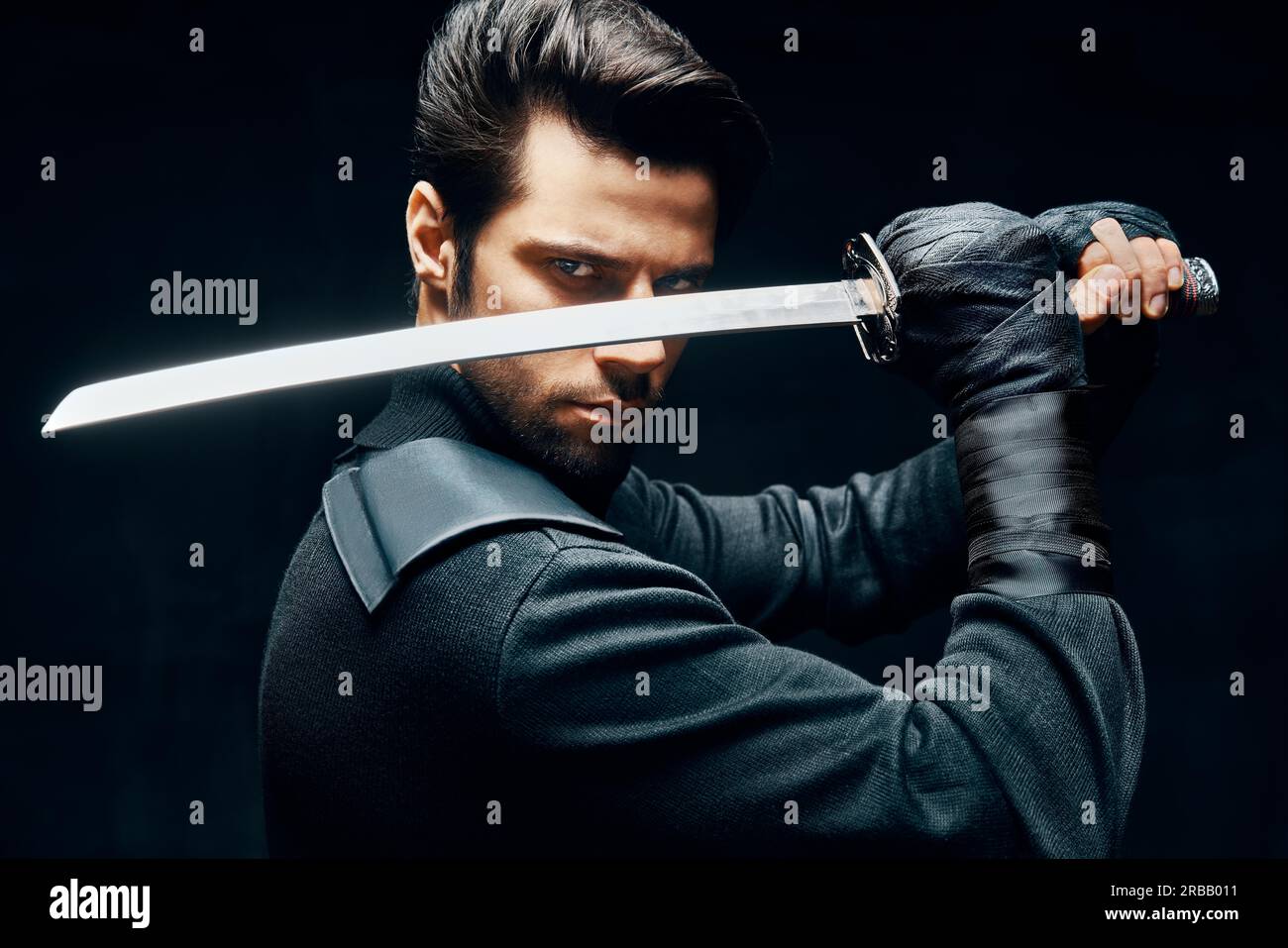 Warrior man posing with a sword ready to stab enemy isolated on black ...