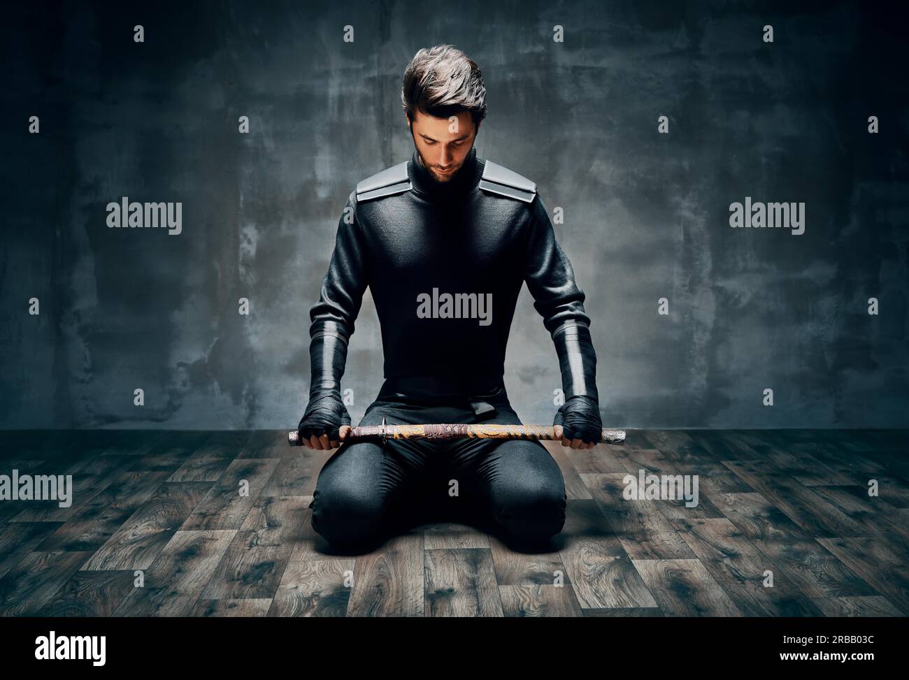 Warrior man sitting on floor posing with a sword over black background ...