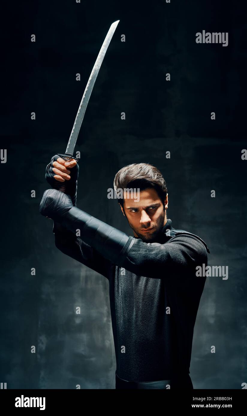 Warrior man posing with a sword ready to stab enemy isolated on black ...