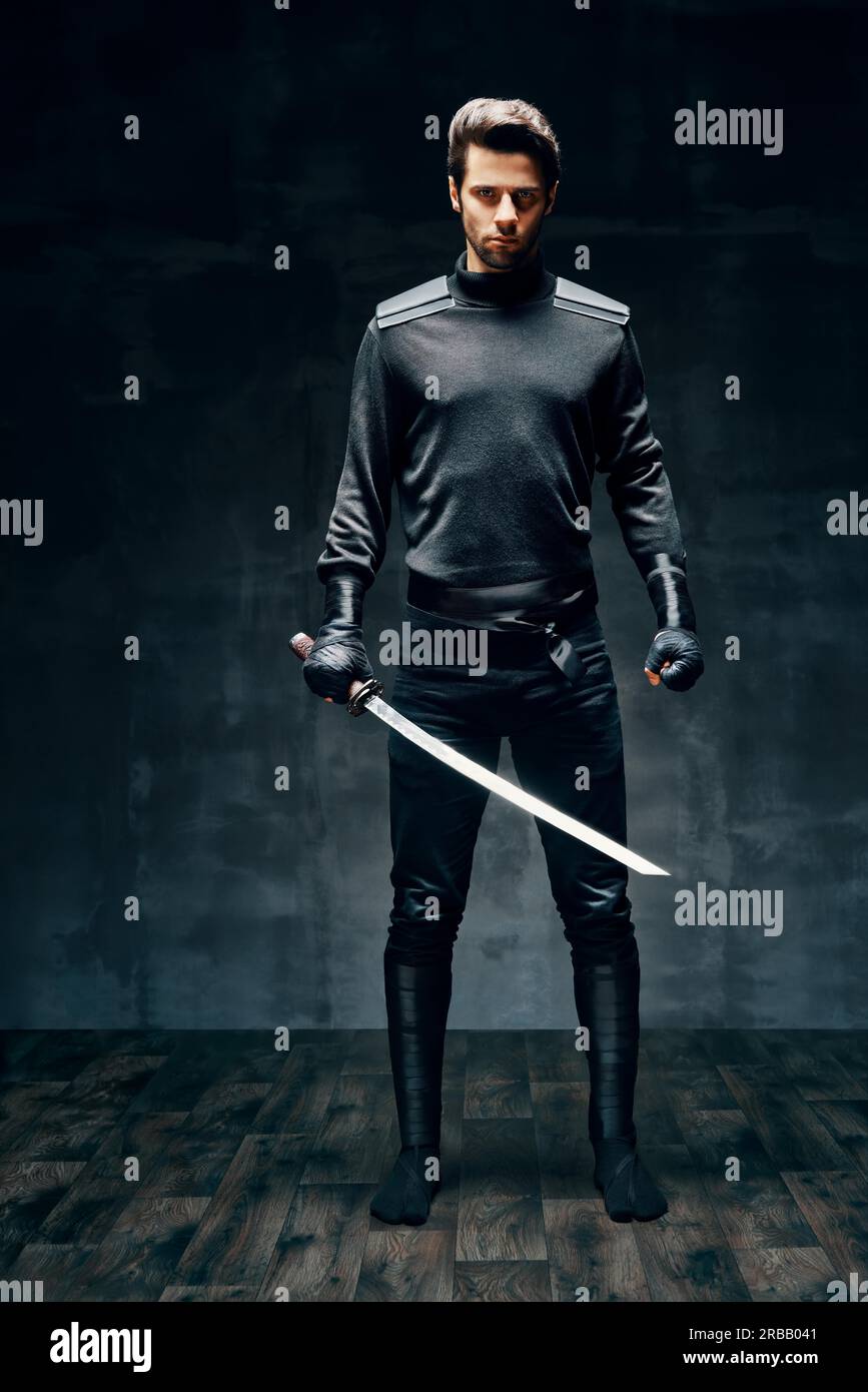 Full length portrait of warrior man posing with a sword over black ...
