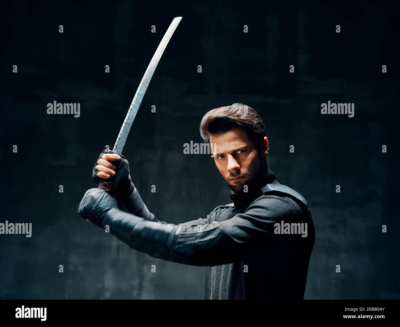 Warrior man posing with a sword ready to stab enemy isolated on black ...