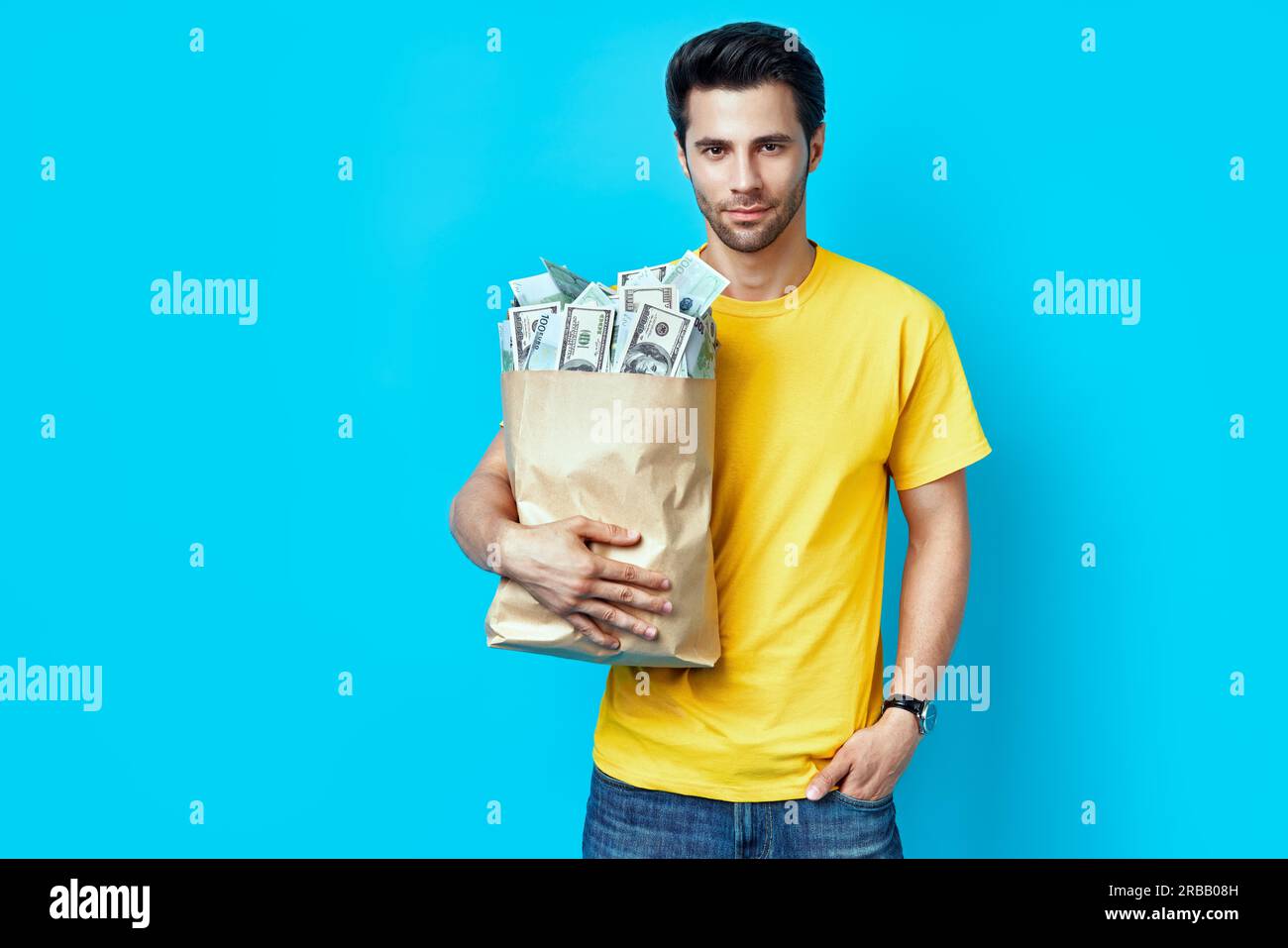 Handsome man hold paper bag full of stacks of money isolated on blue ...