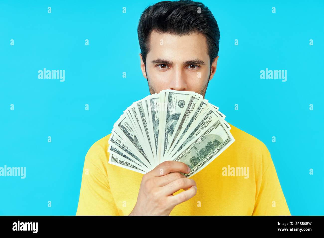 Happy young man holding stack of money and boasting his savings on blue ...